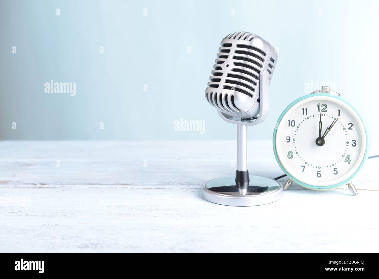 Vintage microphone and alarm clock on table on light blue background ...