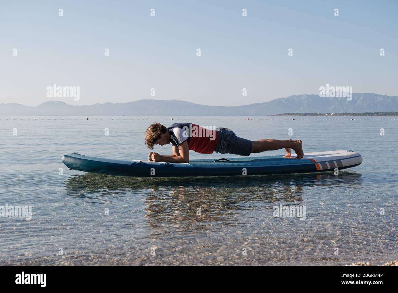 Fit young man working out holding a plank pose on sup board floating on ...