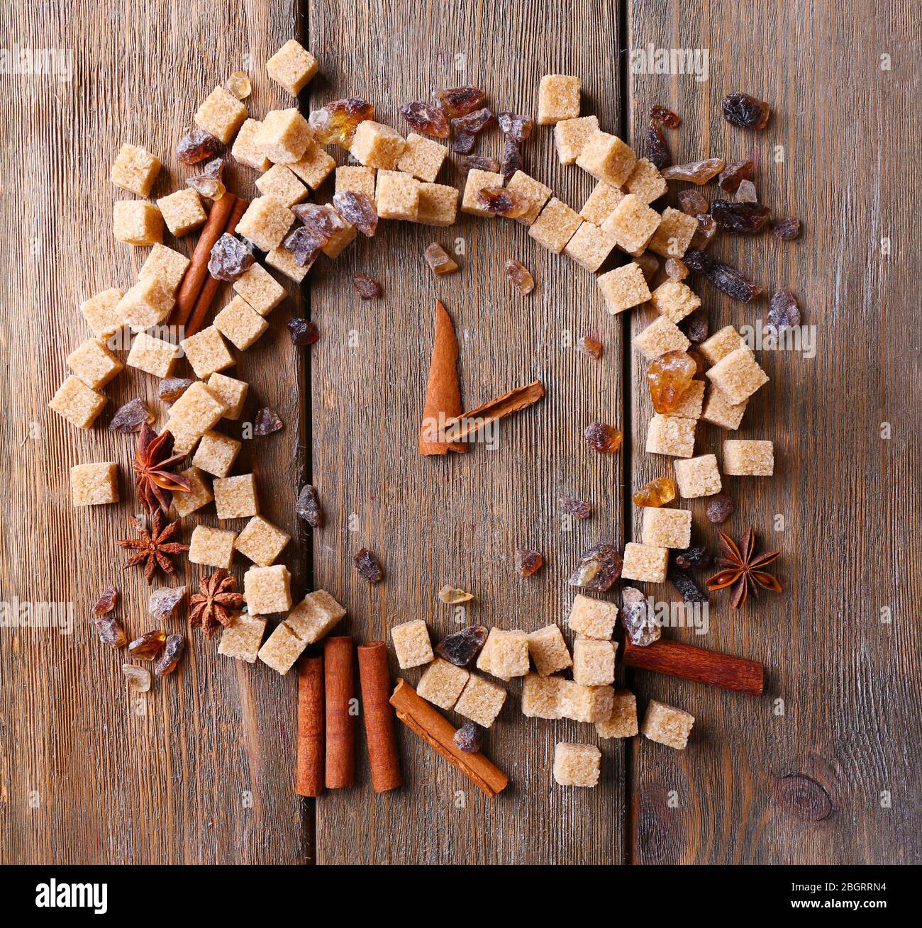 Brown sugar cubes and spices in shape of clock on wooden background ...
