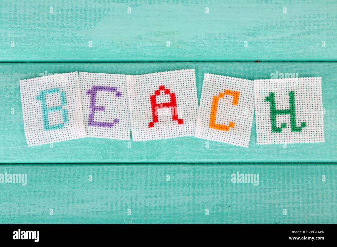 Word made embroidered letters on white fabric, on wooden background ...