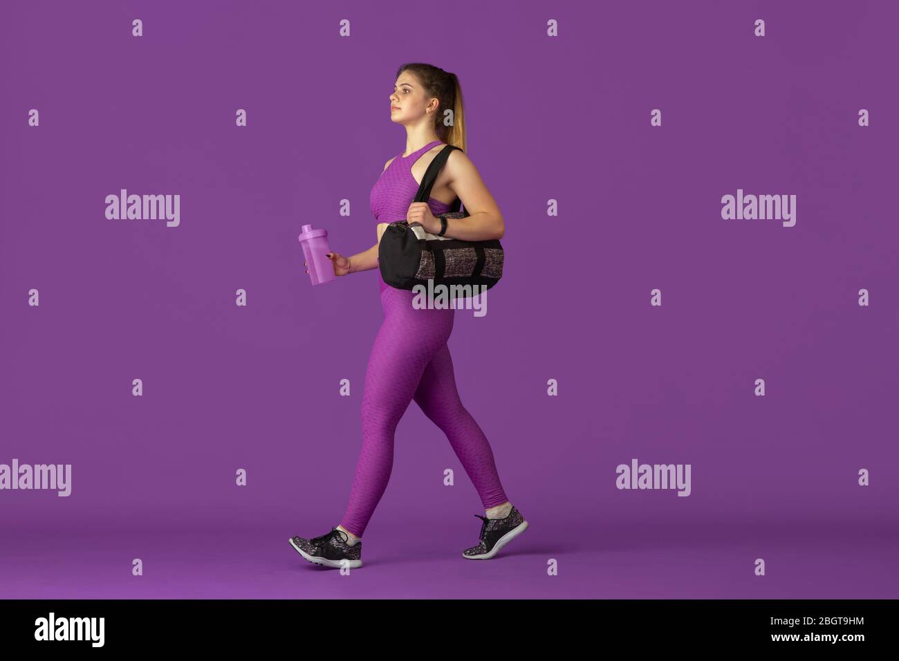 Beautiful young female athlete practicing in studio, monochrome purple ...