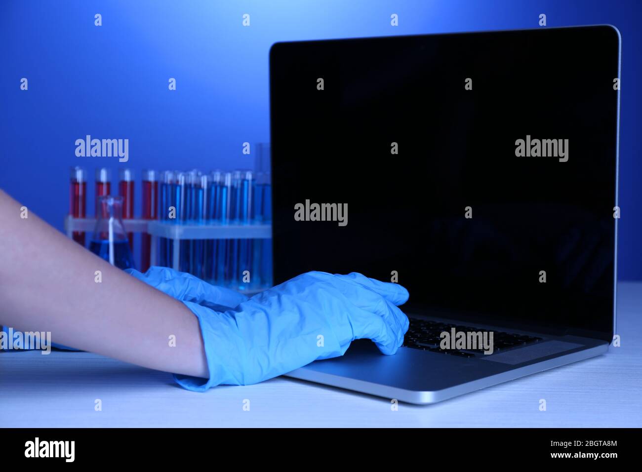 Scientist entering data on laptop computer with test tubes in a ...