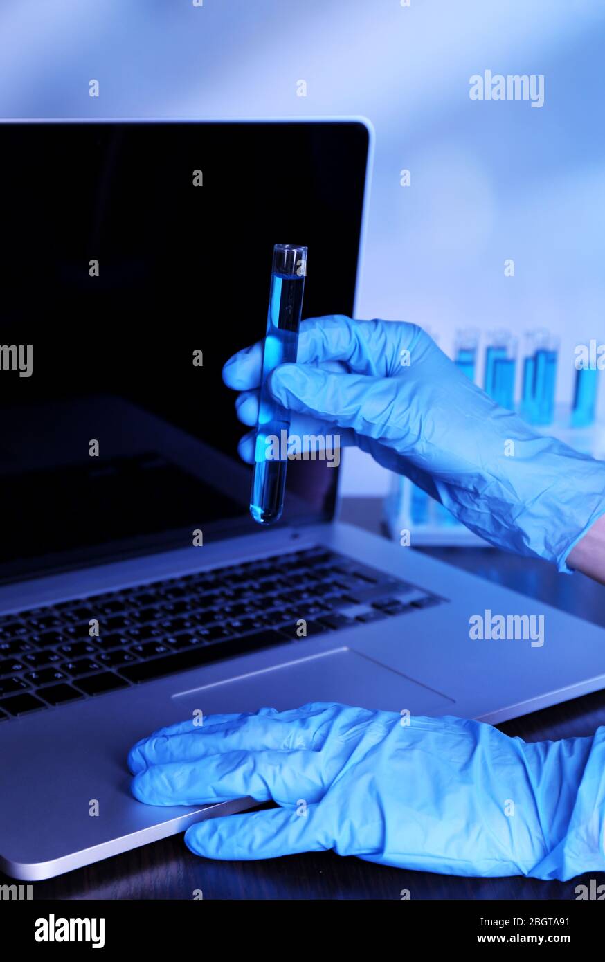 Scientist entering data on laptop computer with test tubes in a ...