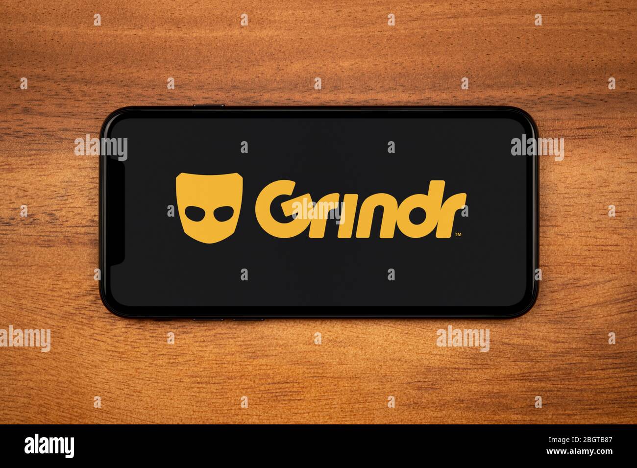 A smartphone showing the Grindr logo rests on a plain wooden table ...