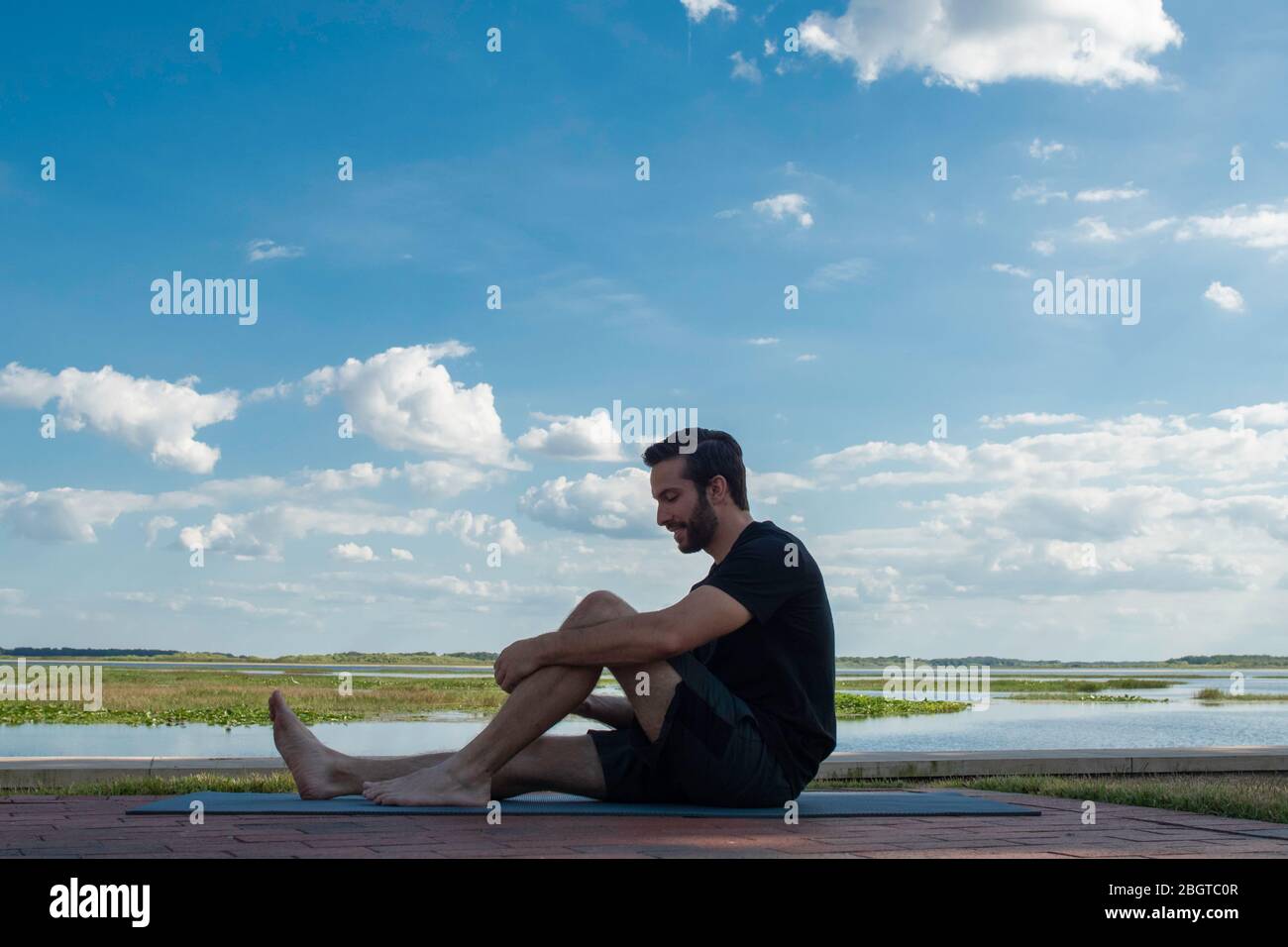 Man wearing a black shirt and dark green shorts bends over in a forward ...