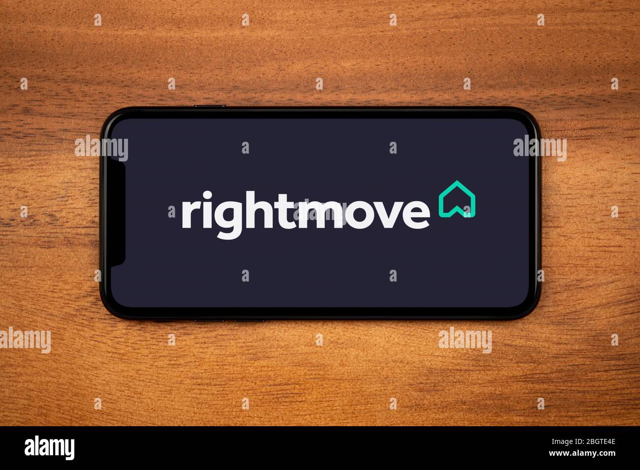 A smartphone showing the Rightmove logo rests on a plain wooden table ...