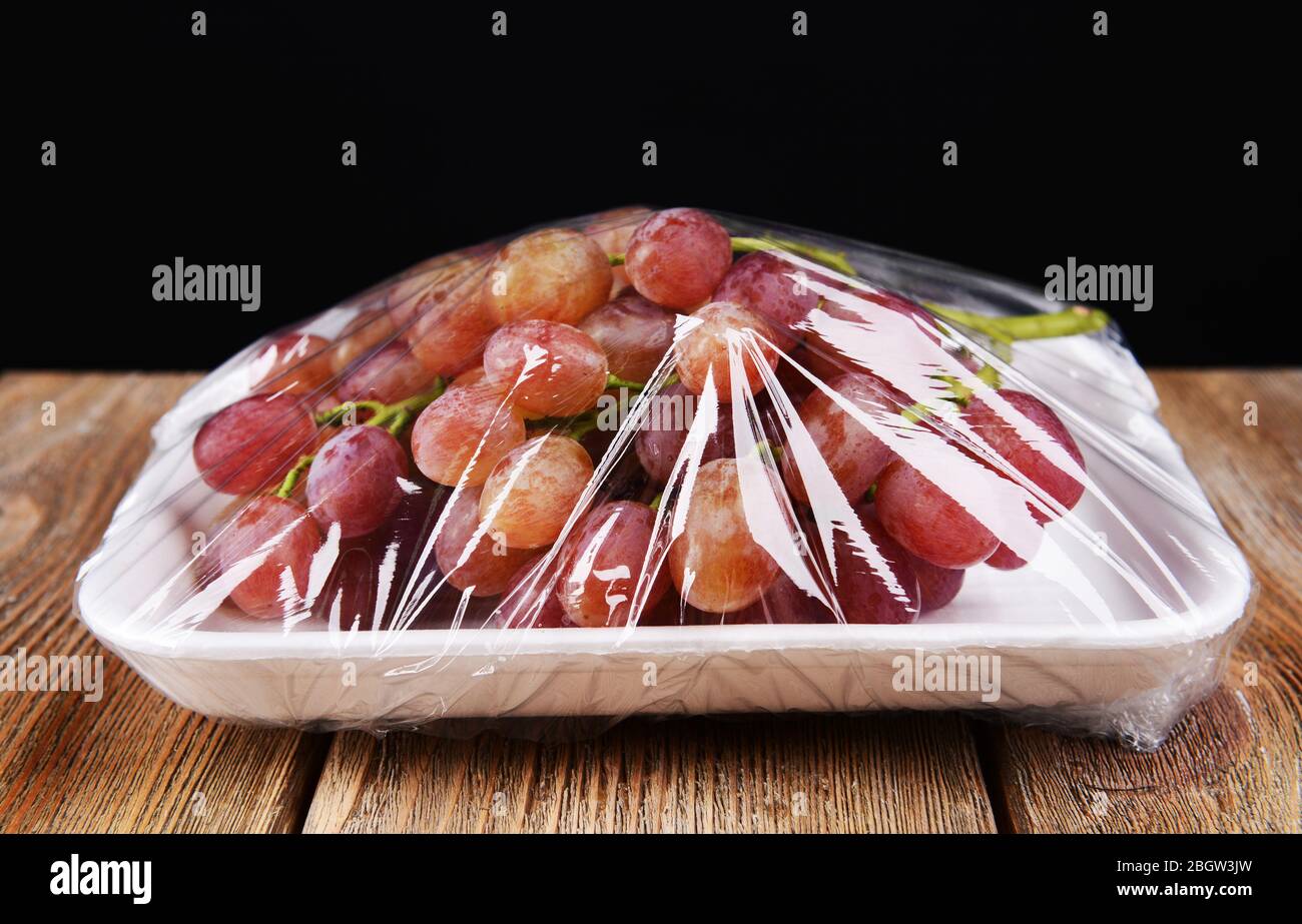 Grapes packed in food film on table on black background Stock Photo - Alamy