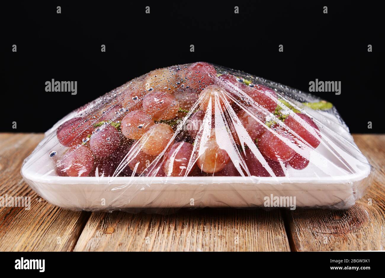 Grapes packed in food film on table on black background Stock Photo - Alamy