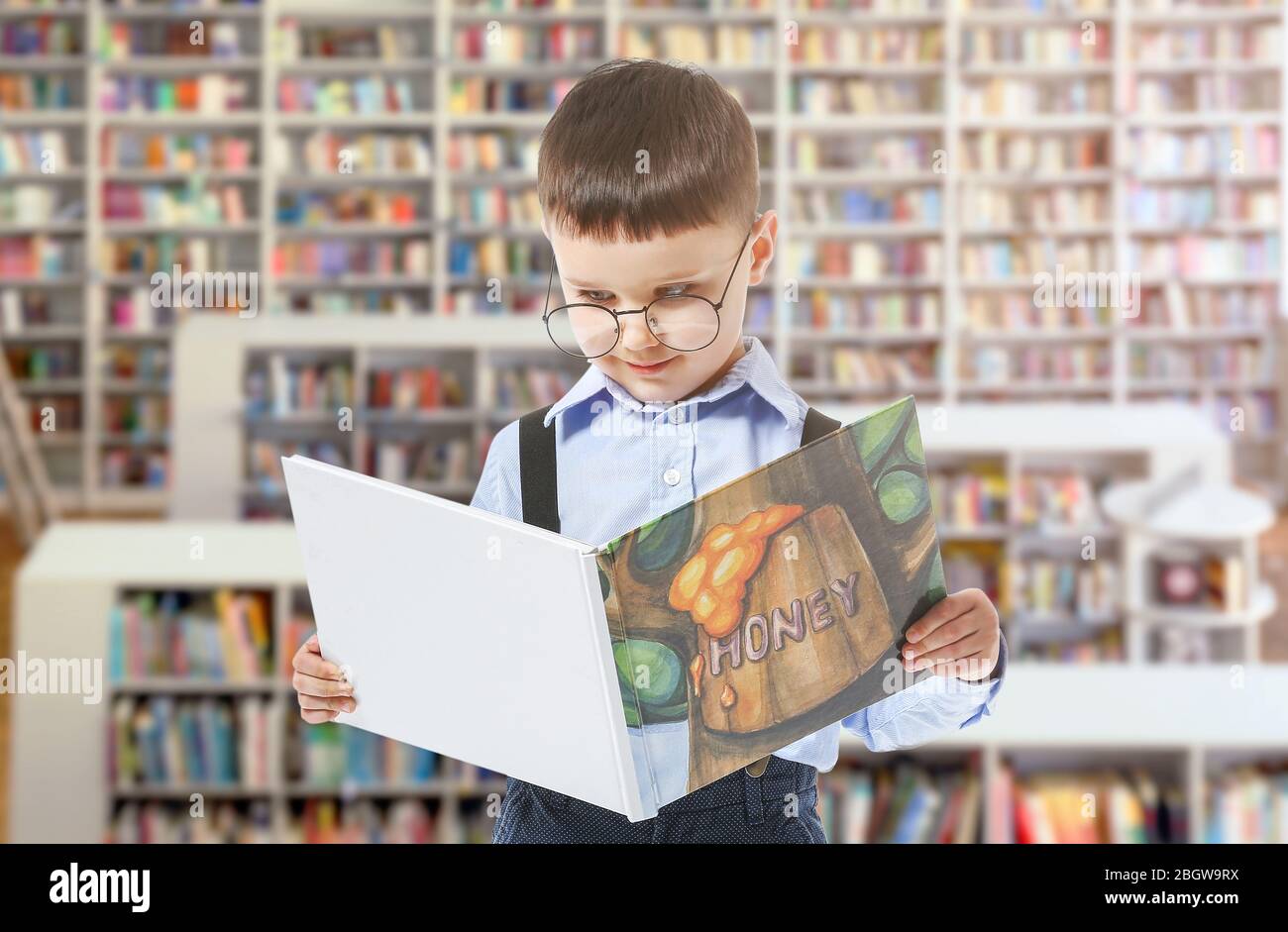 Cute little boy with book in modern library Stock Photo - Alamy