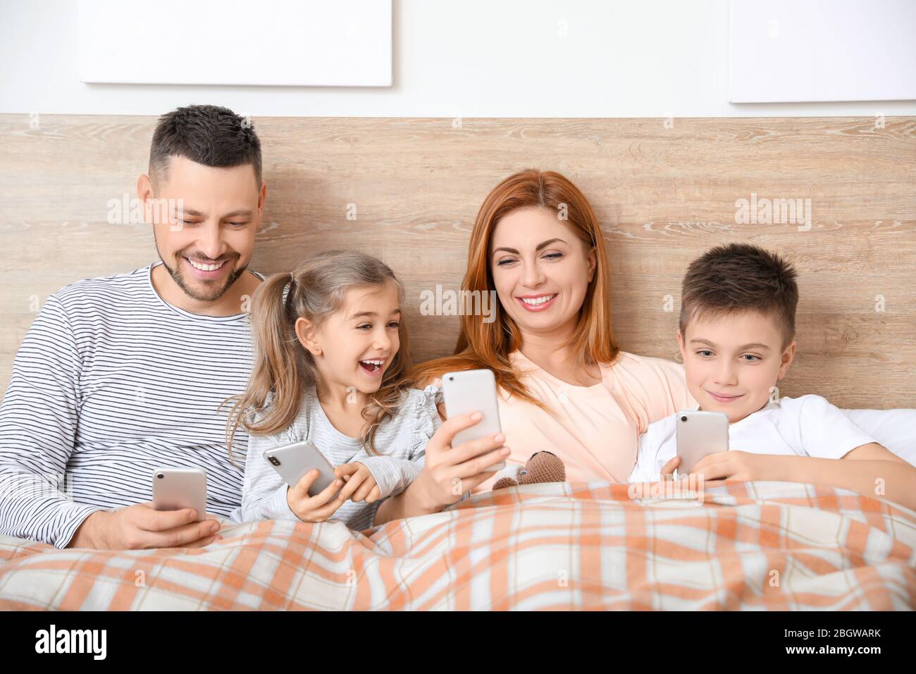 Happy family with mobile phones in bedroom at home Stock Photo - Alamy