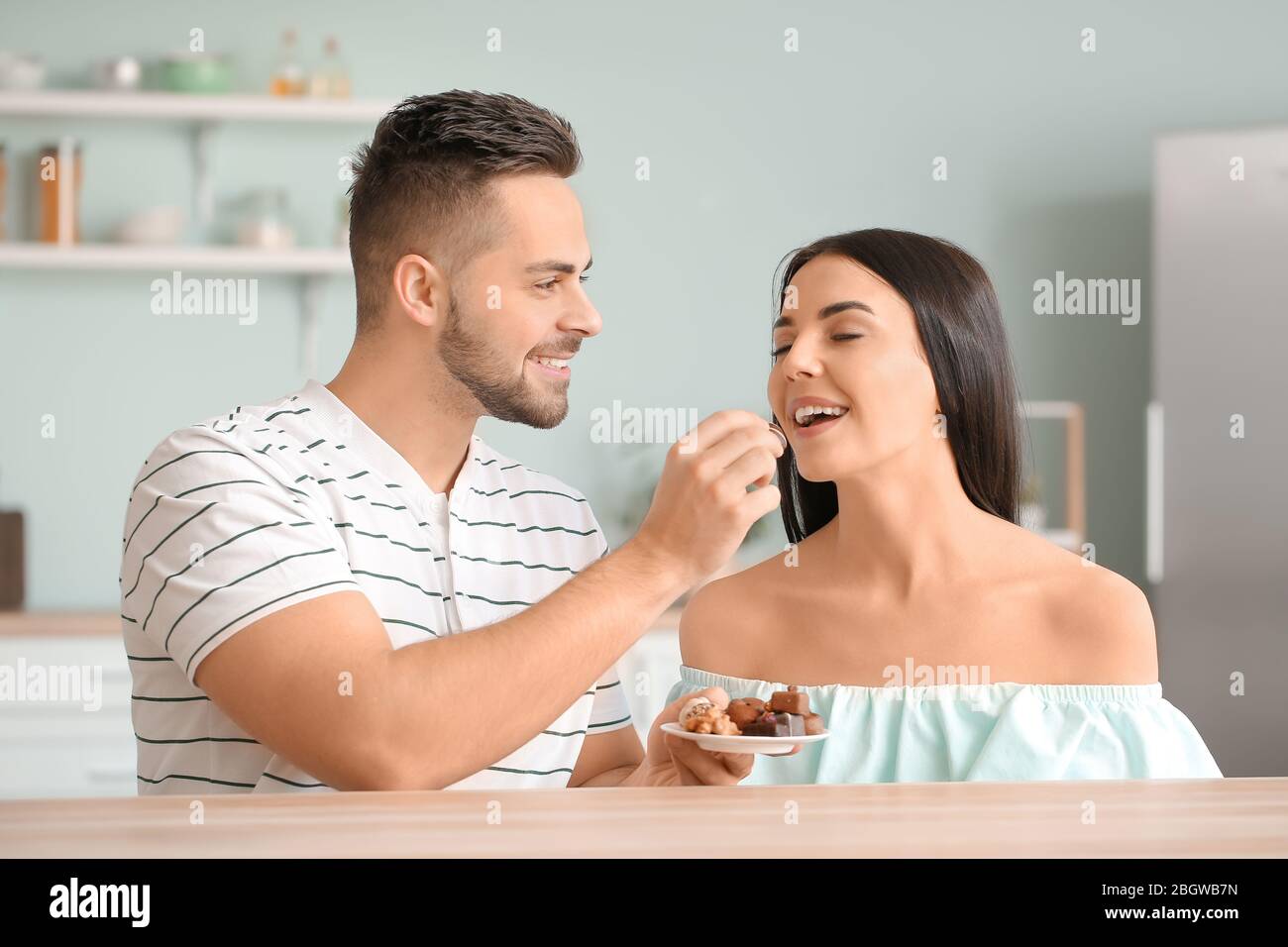 Beautiful young couple eating chocolate in kitchen Stock Photo - Alamy
