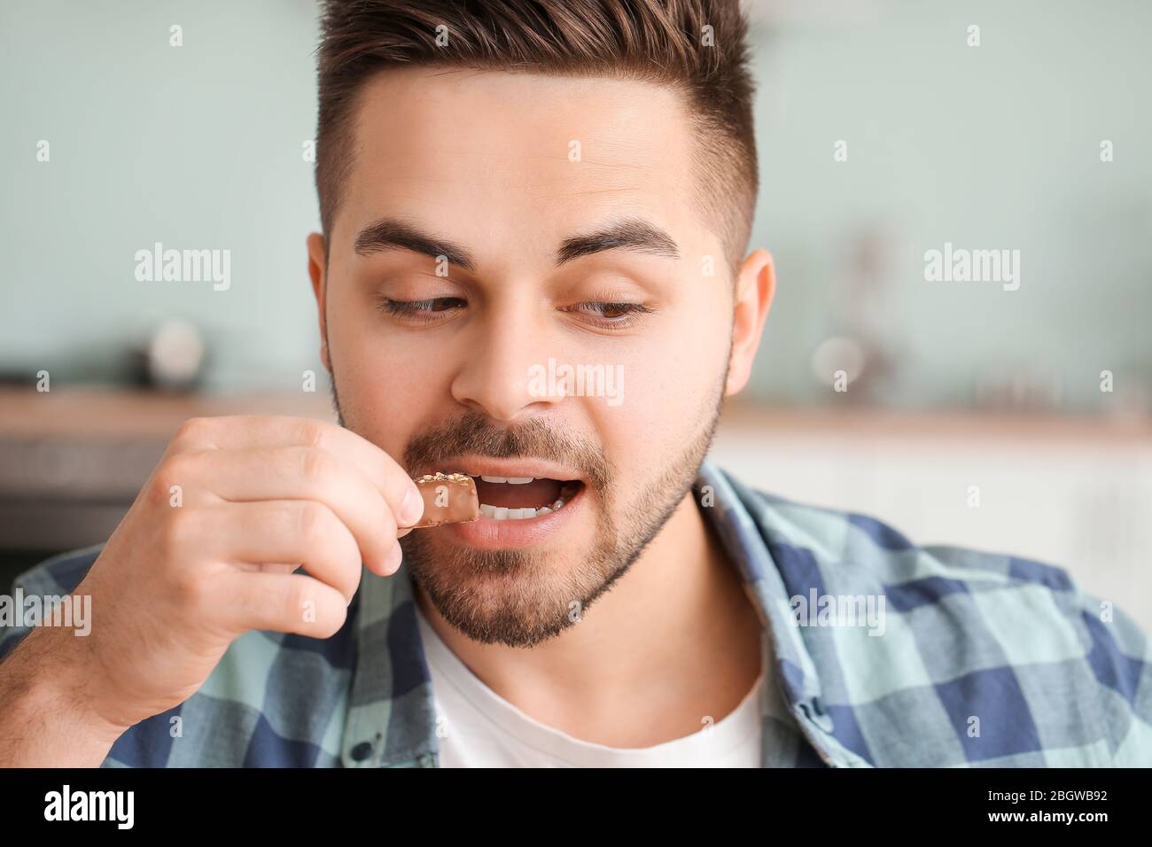 Handsome young man eating chocolate in kitchen Stock Photo - Alamy