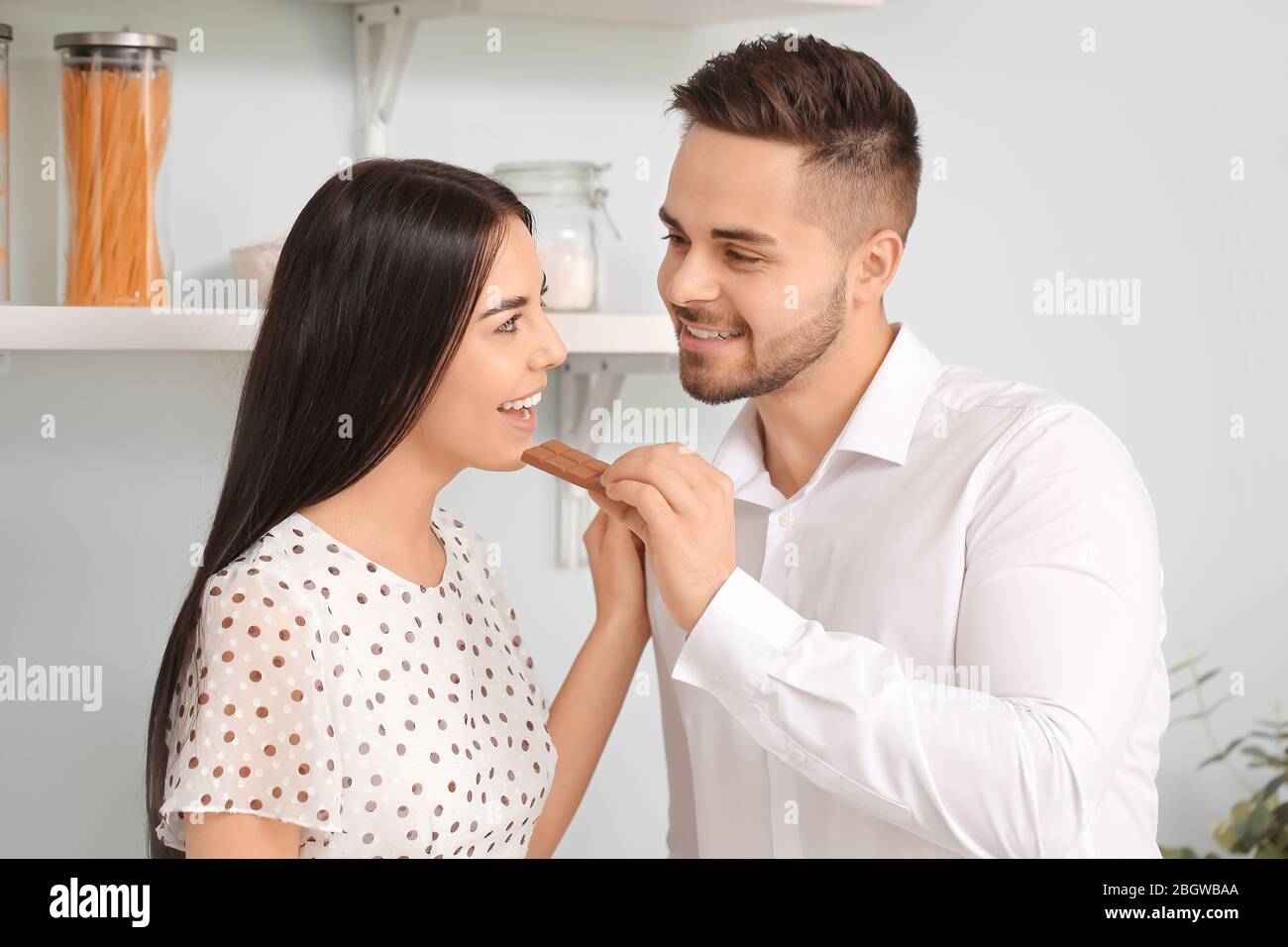 Beautiful young couple eating chocolate in kitchen Stock Photo - Alamy