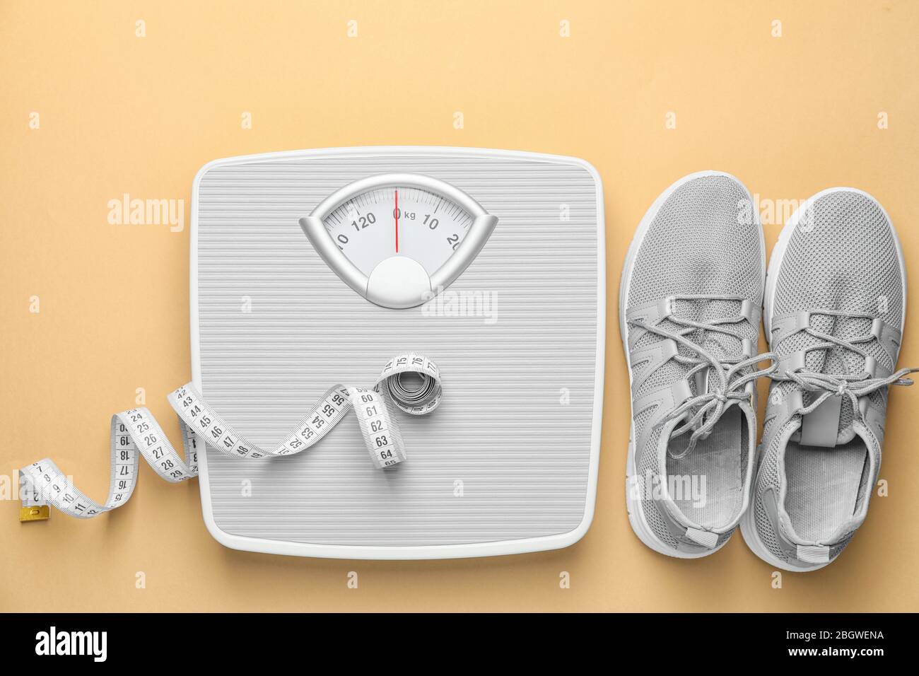 Weight scales with measuring tape and sport shoes on color background ...