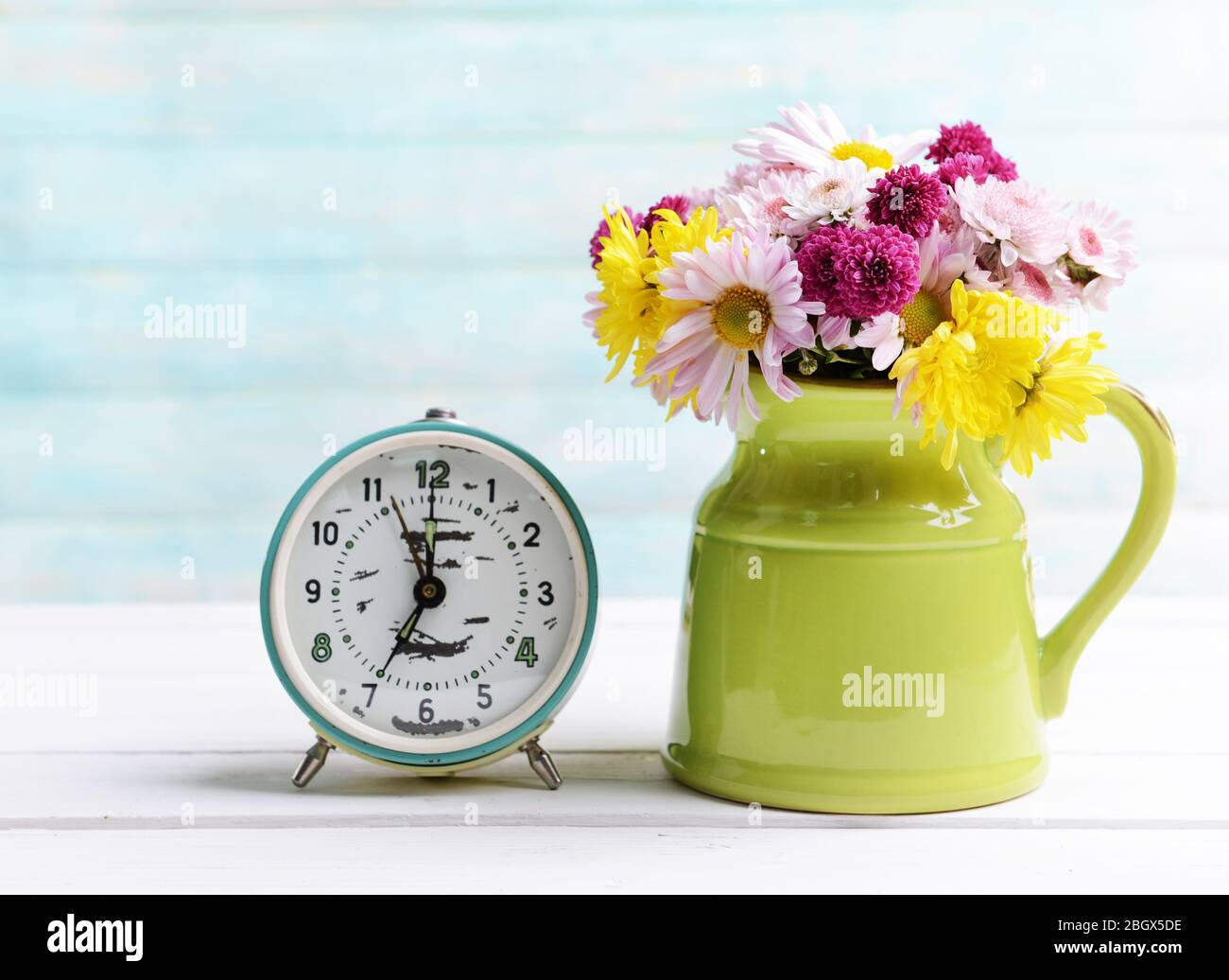 Beautiful flowers in pitcher on table on light blue background Stock ...