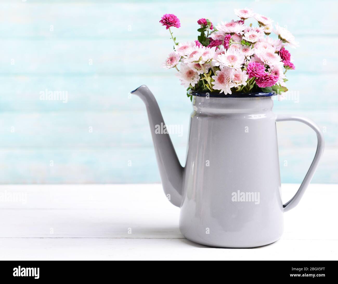 Beautiful flowers in pitcher on table on light blue background Stock ...