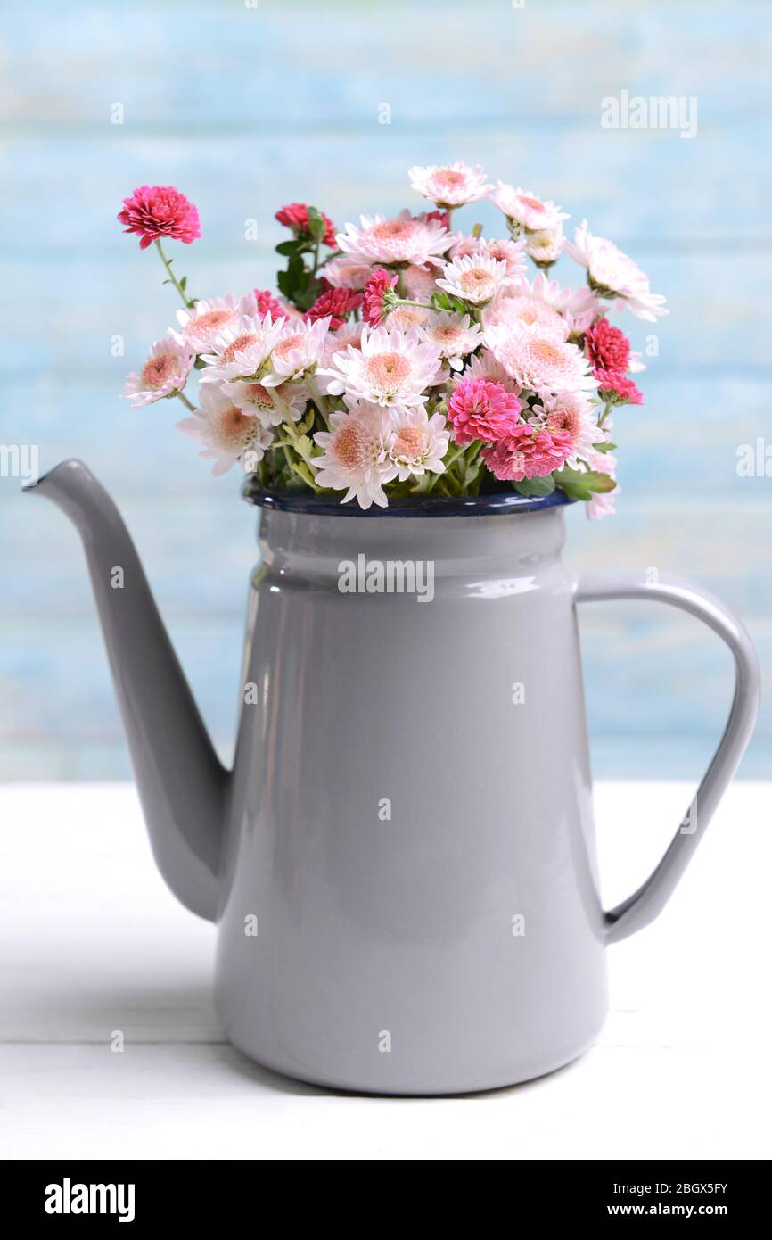 Beautiful flowers in pitcher on table on light blue background Stock ...