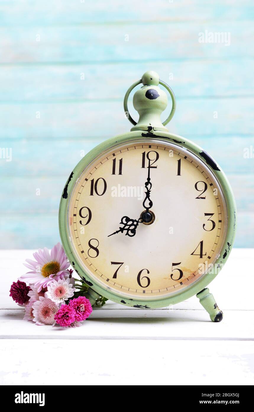 Beautiful flowers with clock on table on light blue background Stock ...