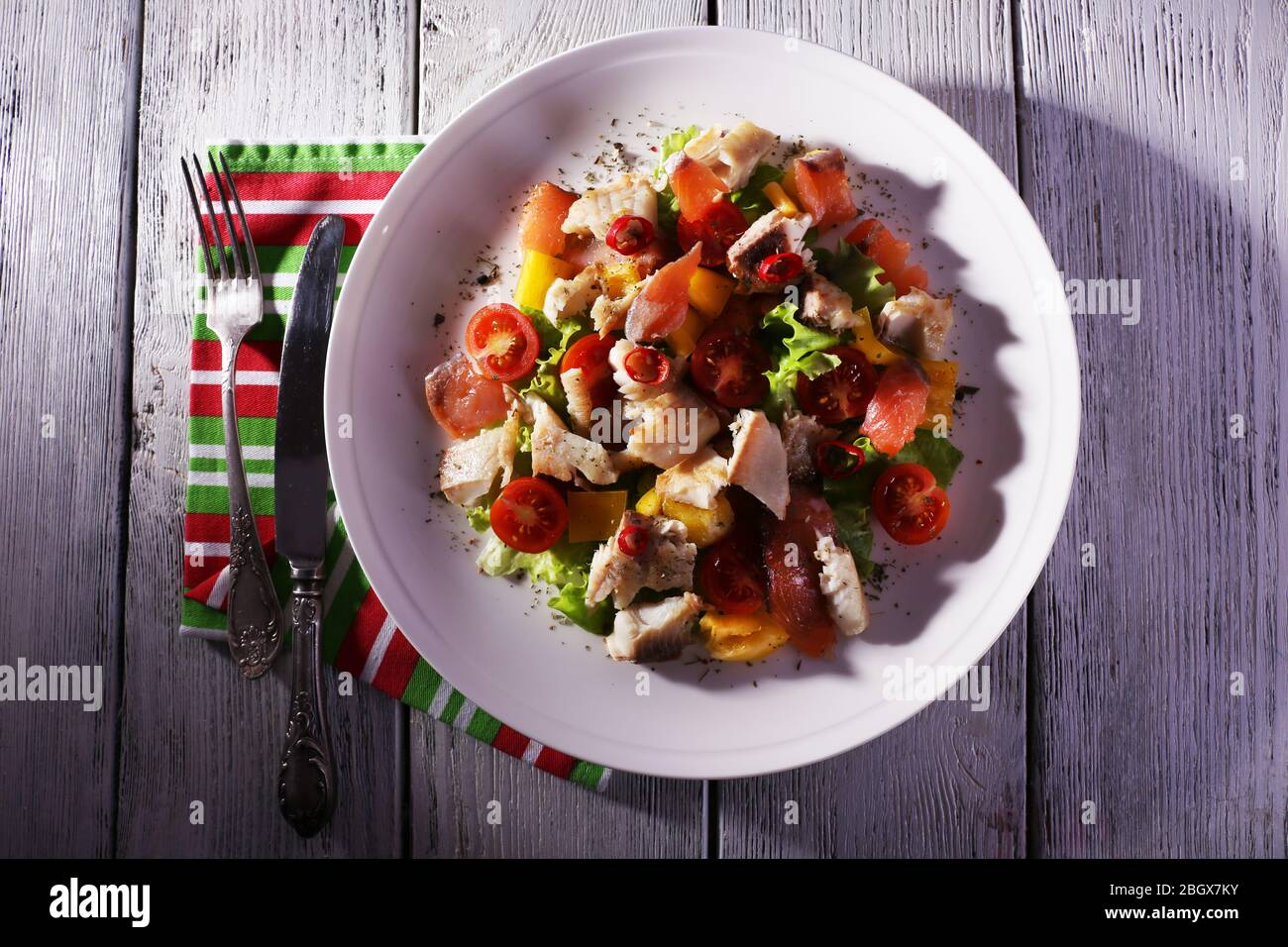 Fresh fish salad with vegetables on plate on wooden table close-up ...
