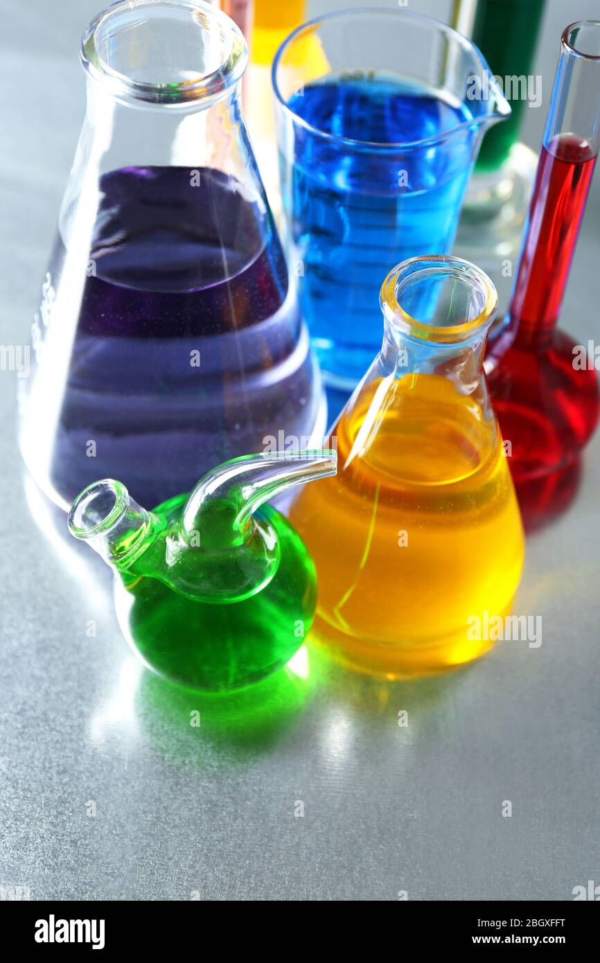 Different laboratory glassware with colorful liquid on color background ...
