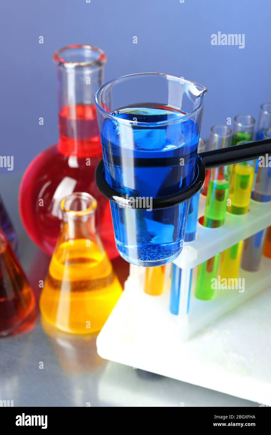 Different laboratory glassware with colorful liquid on color background ...