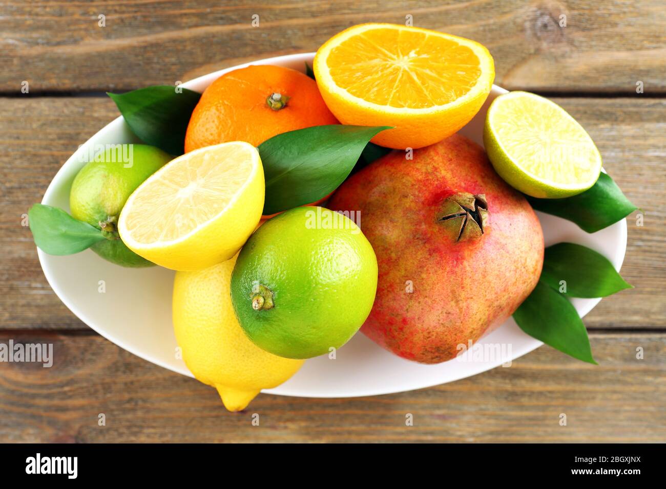 Ripe citrus with green leaves on plate on wooden background Stock Photo ...