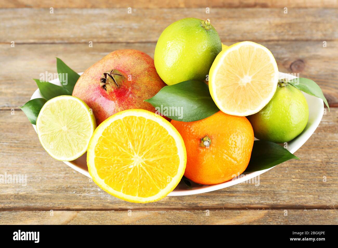 Ripe citrus with green leaves on plate on wooden background Stock Photo ...