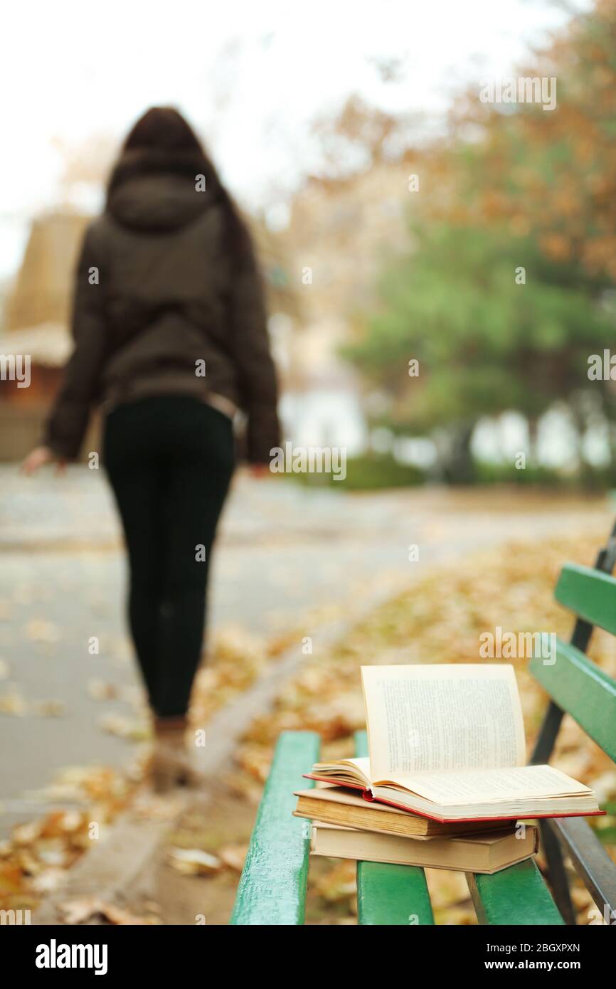 Book left on the bench with silhouette of girl walking away in autumn ...