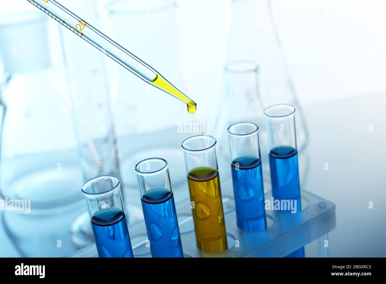 Pipette adding yellow fluid to one of several test-tubes with flasks on ...