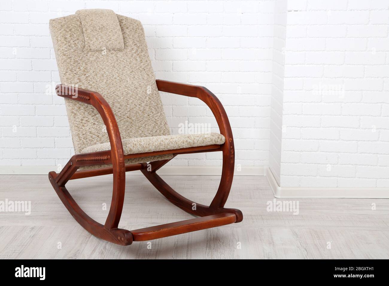 Comfortable rocking-chair on wooden floor near brick wall background ...