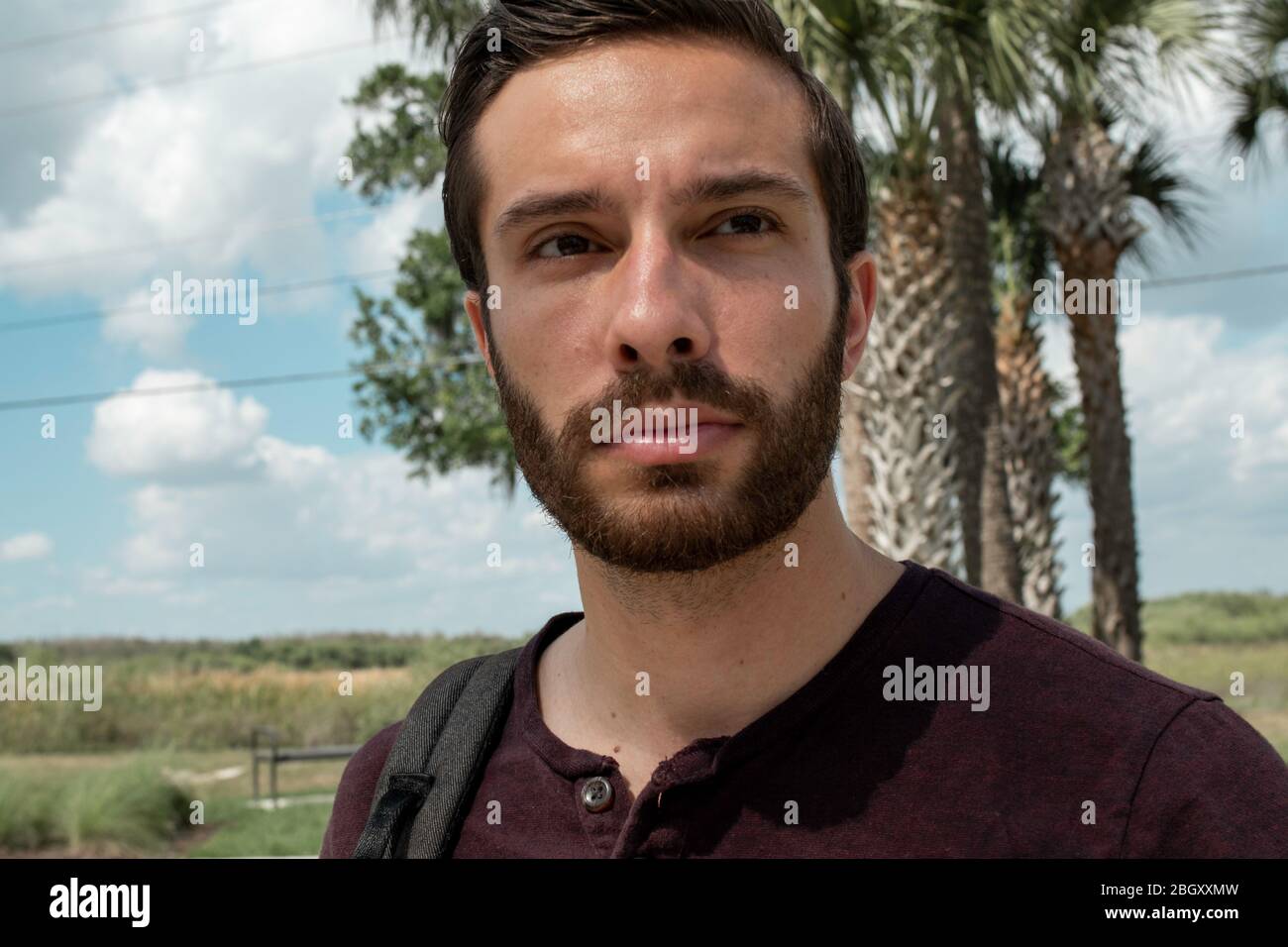 A close up of a man with natural blemished skin wearing a red shirt ...
