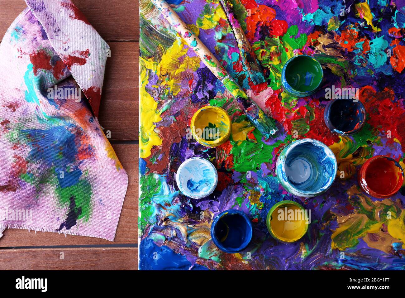 Abstract painting on canvas with cans, brush and rag on wooden table ...