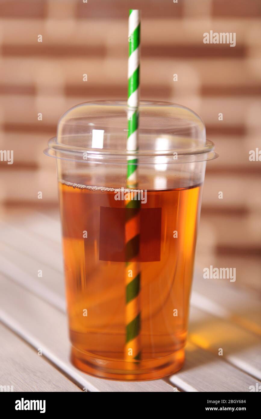 Apple juice in fast food closed cup with tube on wooden table and brick ...