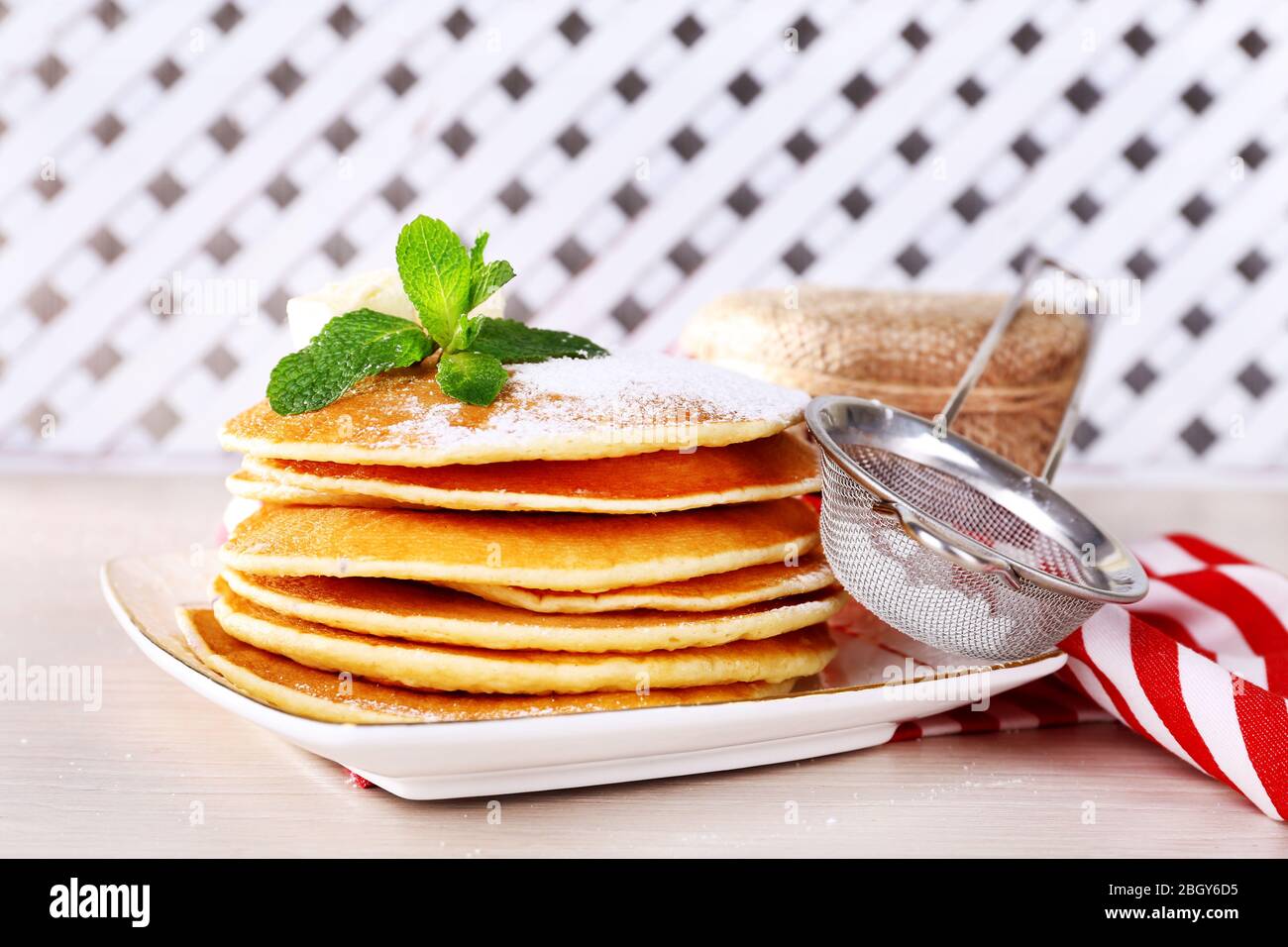 Stack of pancakes on plate with bank of jam on table and wooden lattice ...