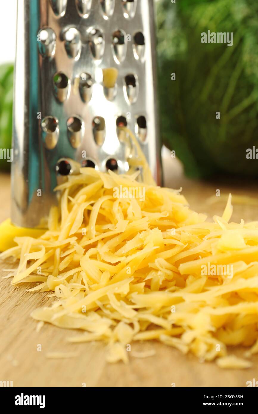 Grated cheese with grater and vegetables on wooden cutting board and ...