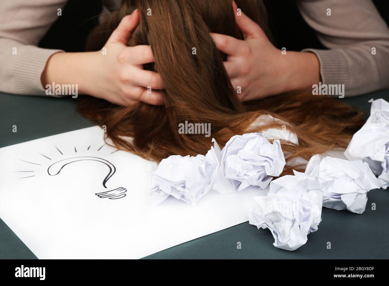Tired woman at desk with question mark sheet of paper, on dark ...
