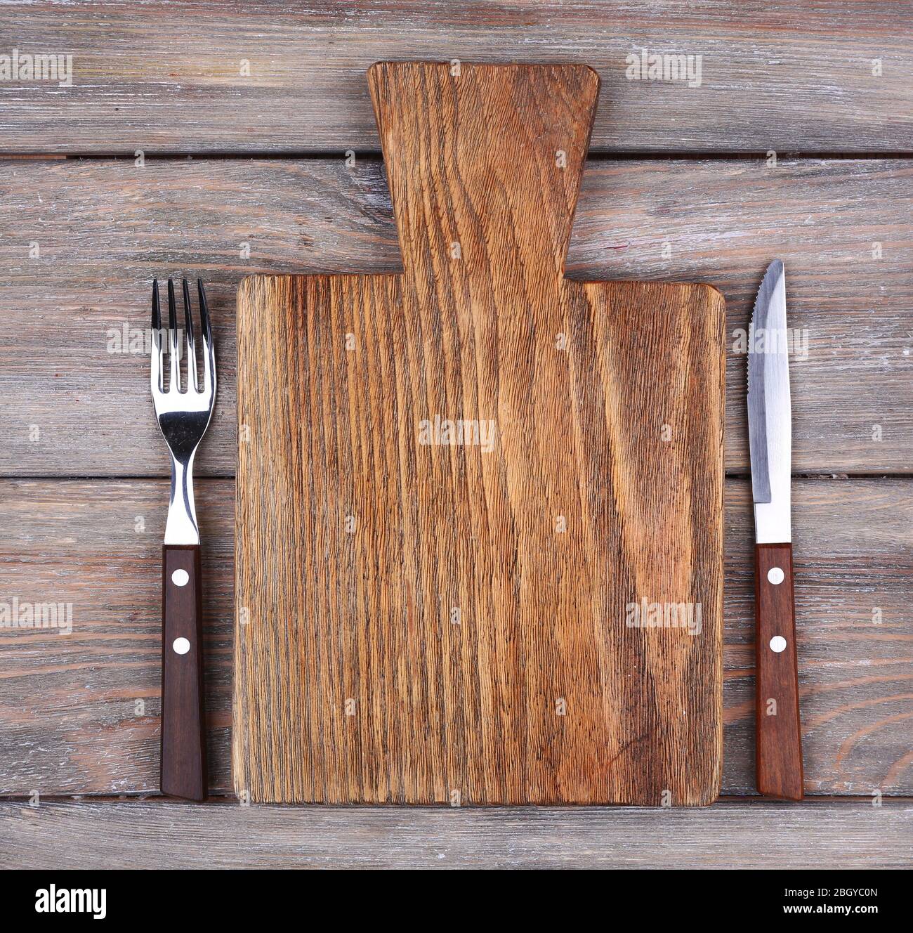 Cutting board with fork and knife on rustic wooden planks background ...