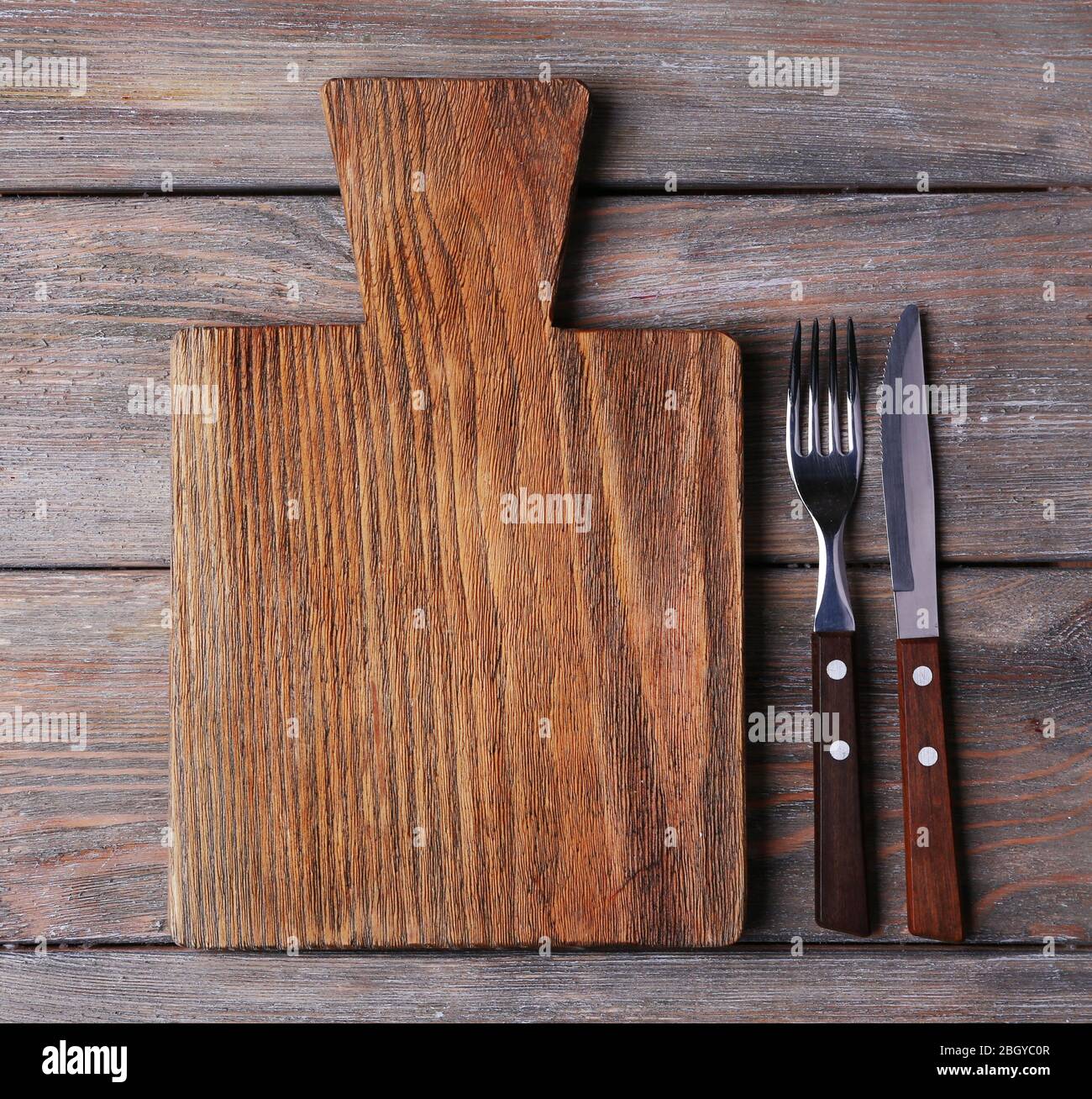 Cutting board with fork and knife on rustic wooden planks background ...