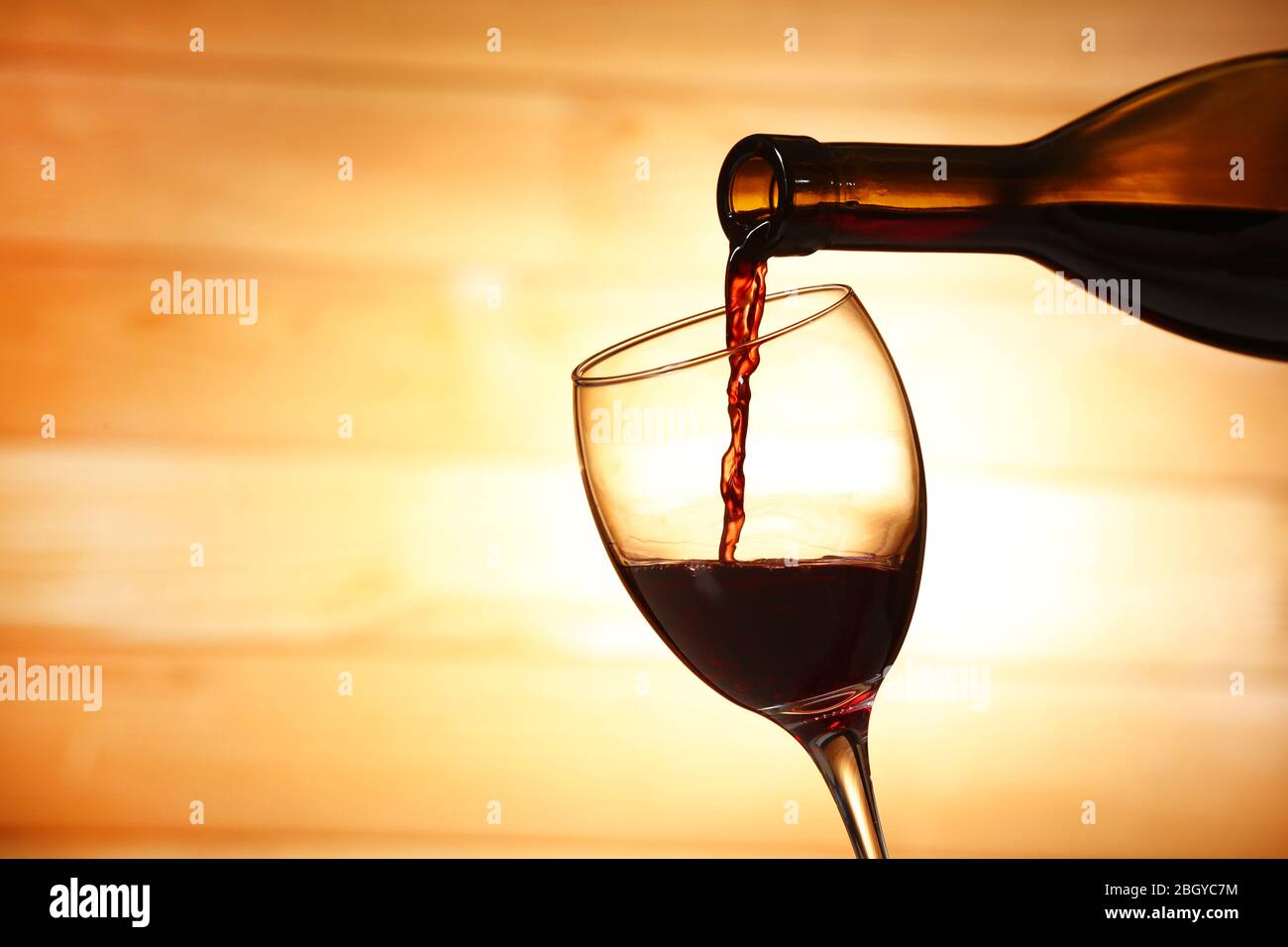Pouring red wine from bottle into glass on wooden planks background ...