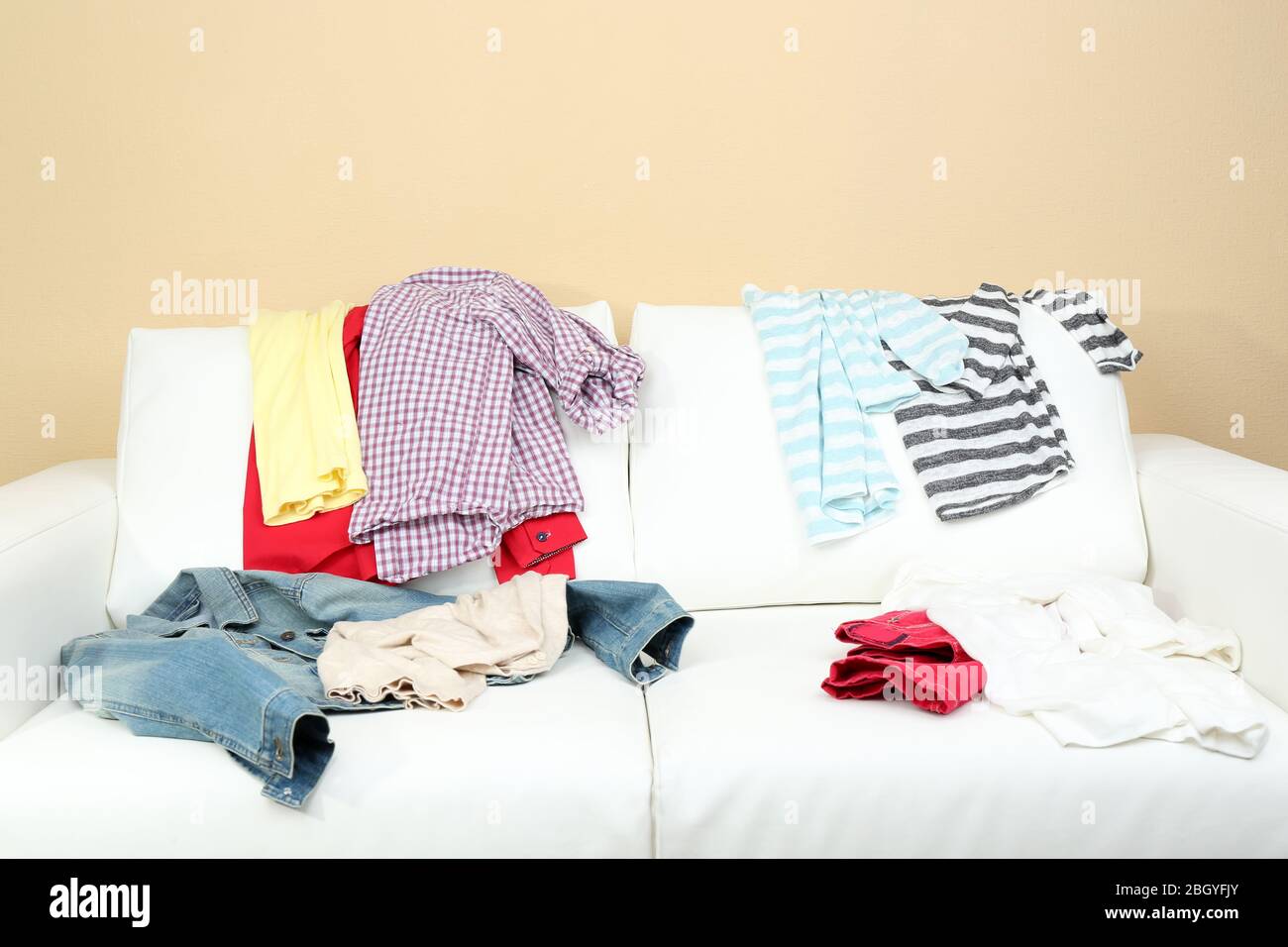 Messy clothing on white sofa, on light wall background Stock Photo - Alamy