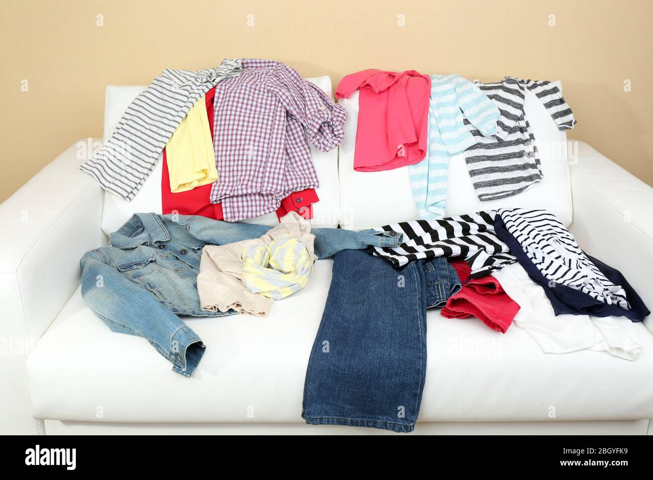 Messy clothing on white sofa, on light wall background Stock Photo - Alamy