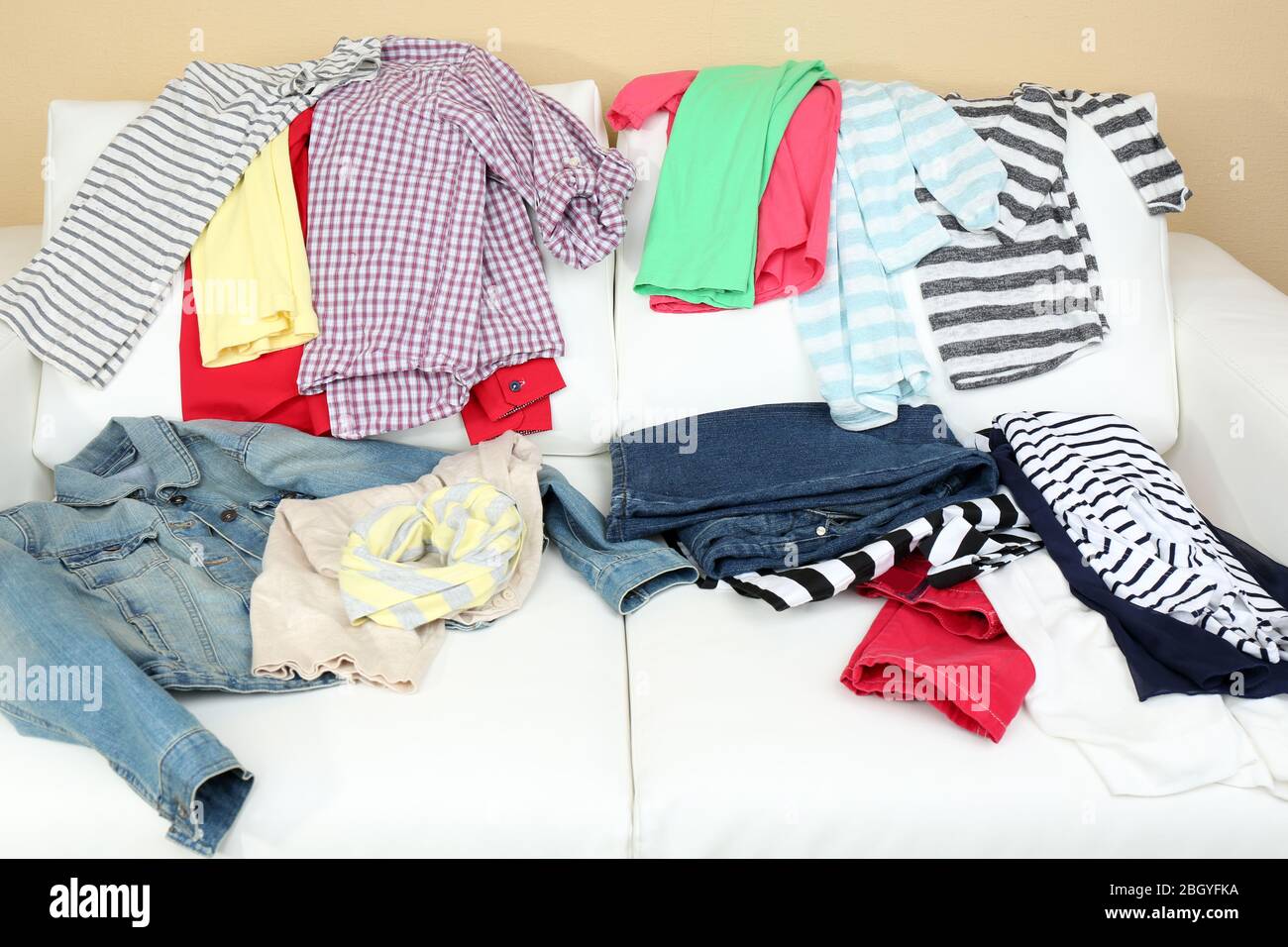Messy clothing on white sofa, on light wall background Stock Photo - Alamy