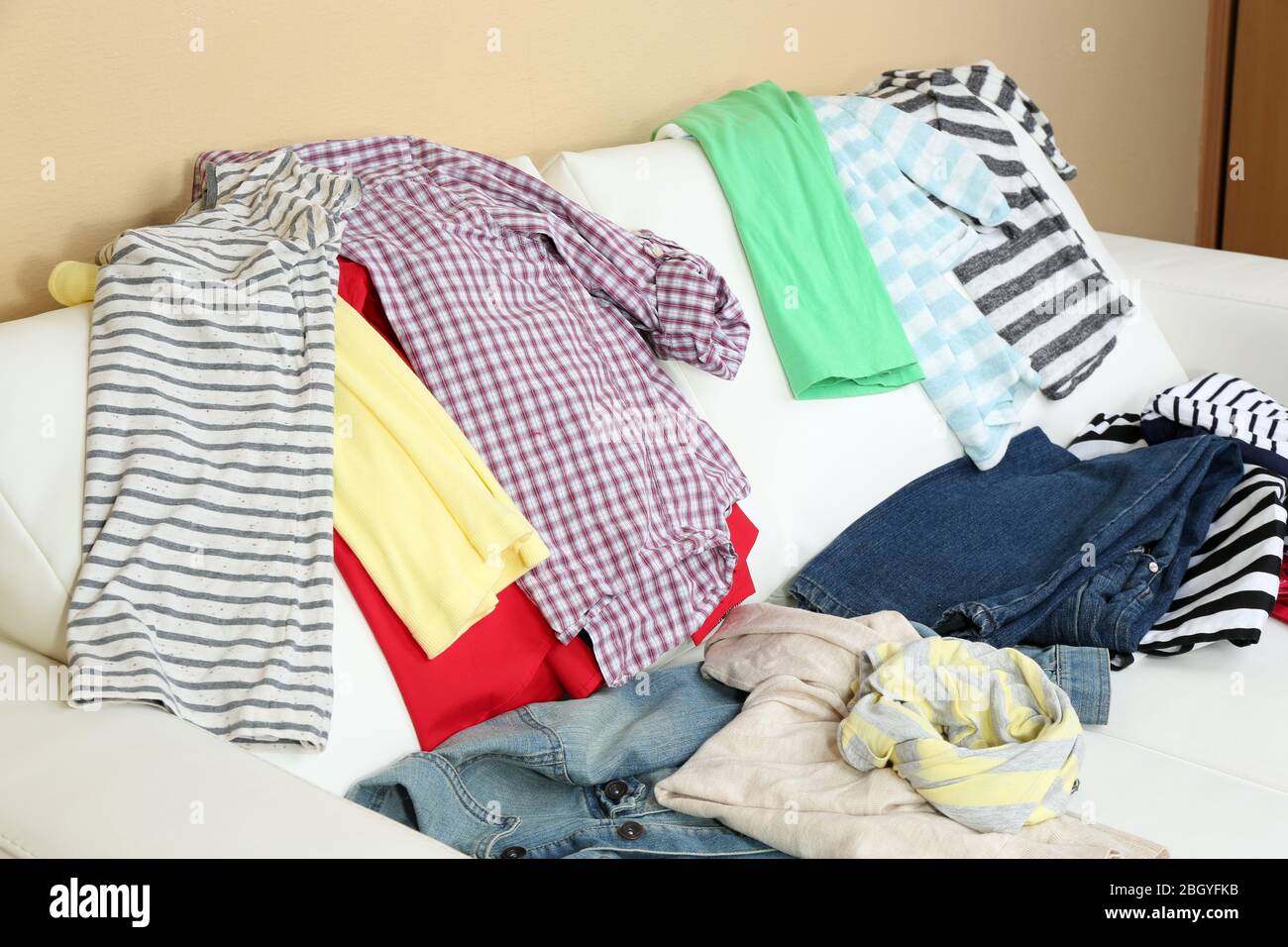 Messy clothing on white sofa, on light wall background Stock Photo - Alamy