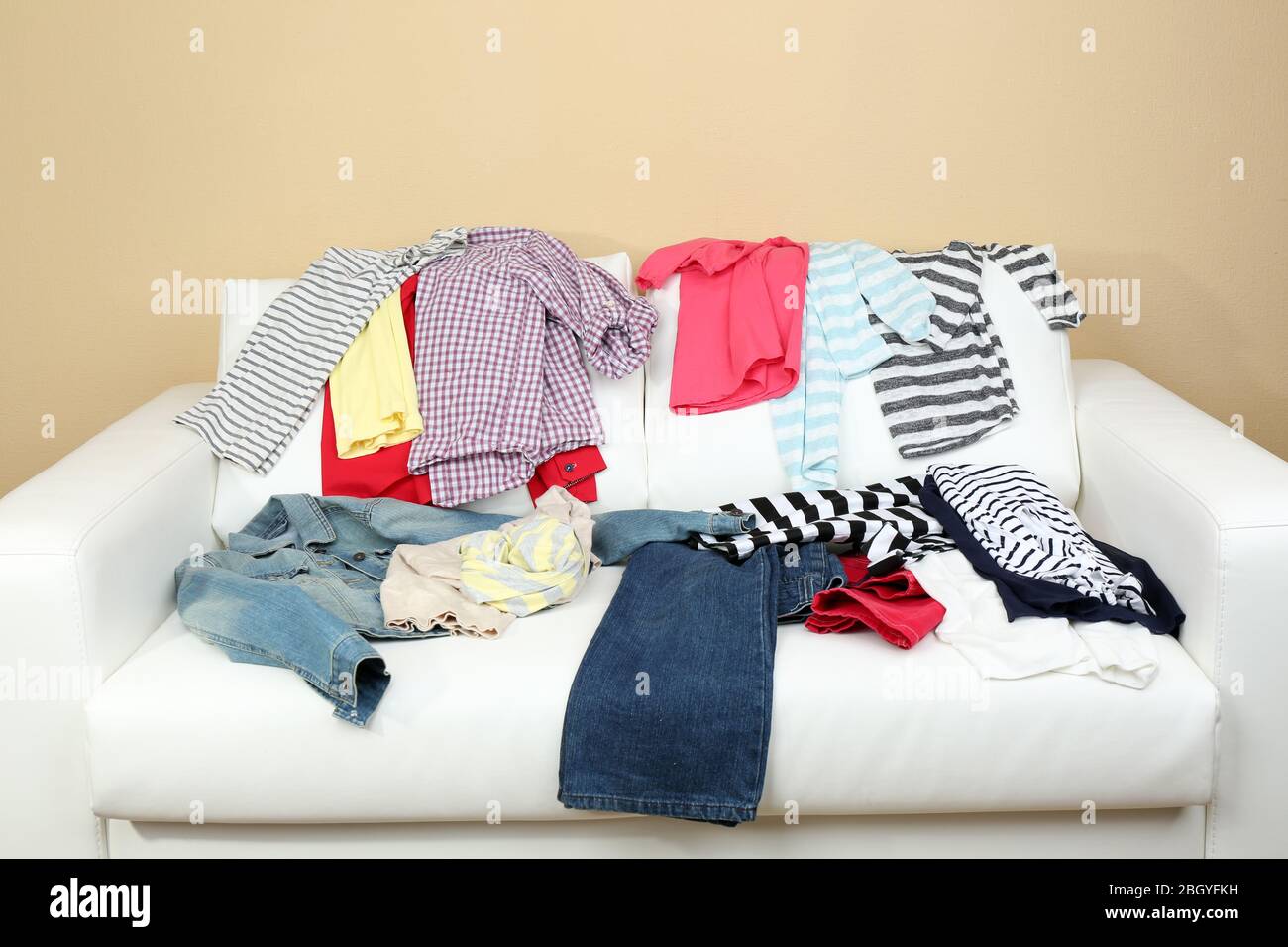 Messy clothing on white sofa, on light wall background Stock Photo - Alamy