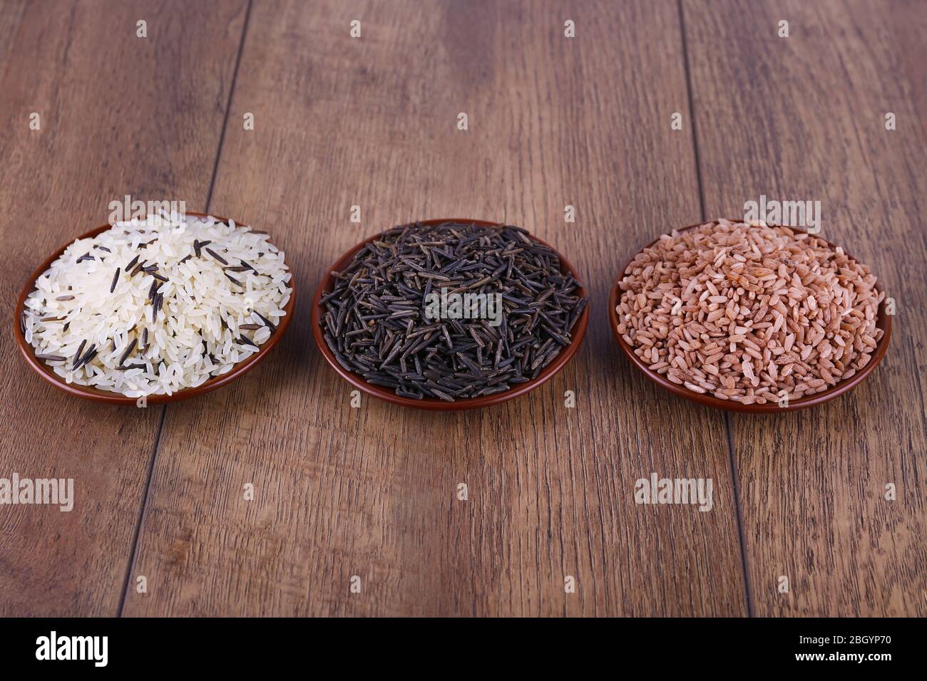 Different kinds of rice on plates on wooden background Stock Photo - Alamy