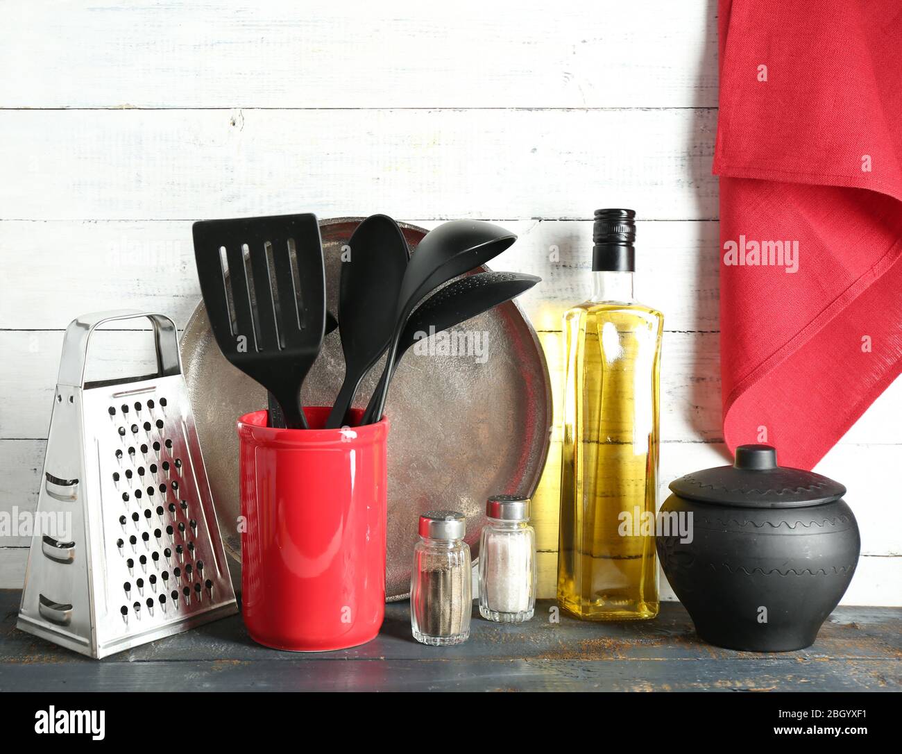 Plastic kitchen utensils in red cup with bottle of olive oil on wooden ...