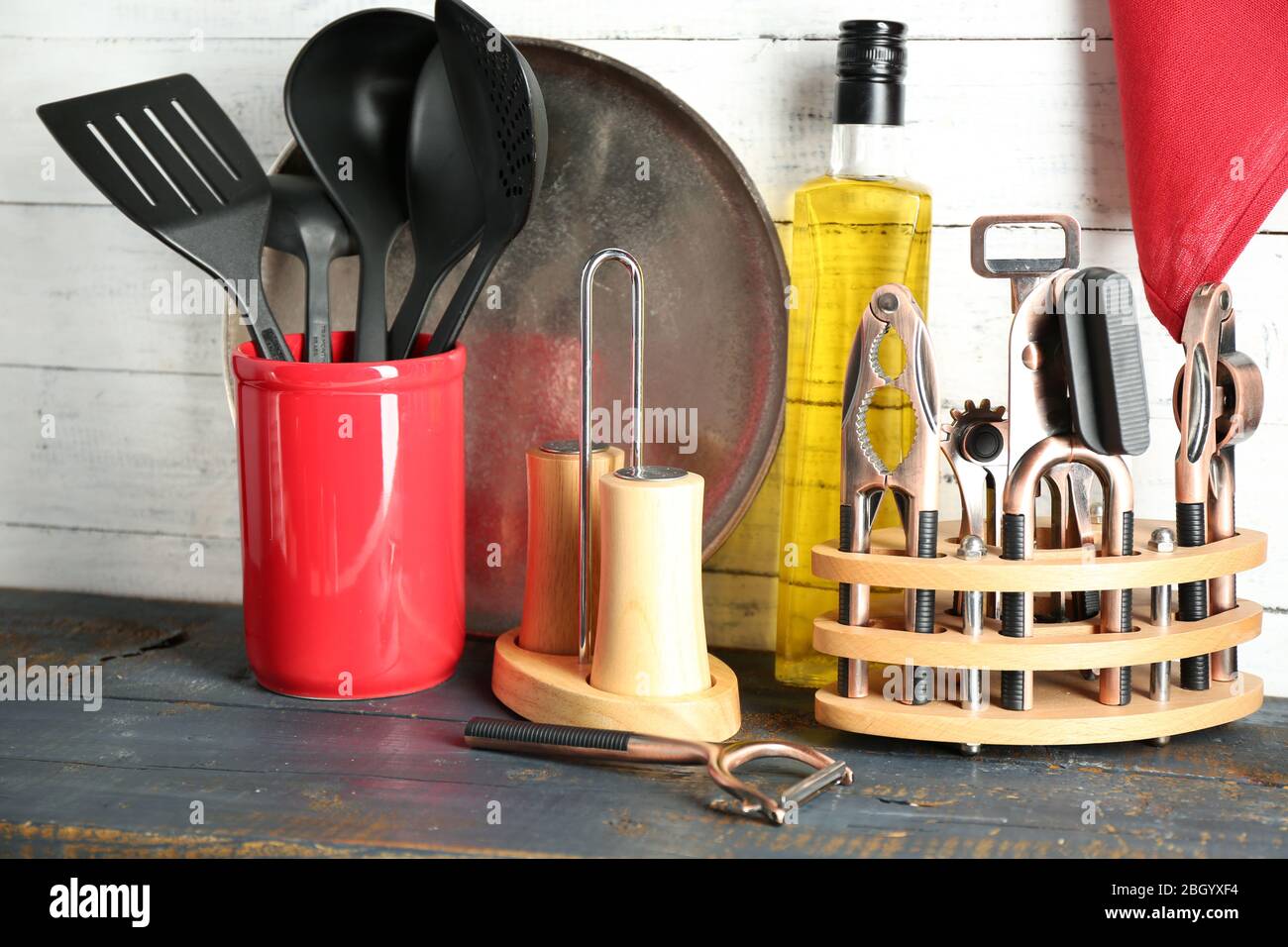 Plastic kitchen utensils in red cup with bottle of olive oil on wooden ...