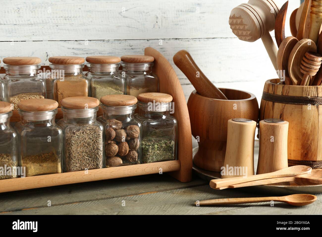Different spices in glass bottles on stand with utensils on wooden ...