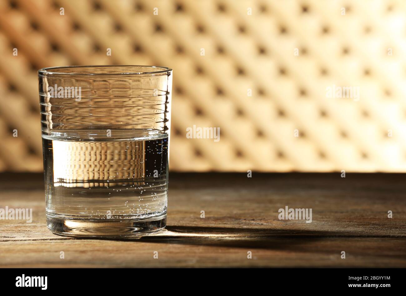 Glass of clean mineral water on wooden surface and lattice background ...