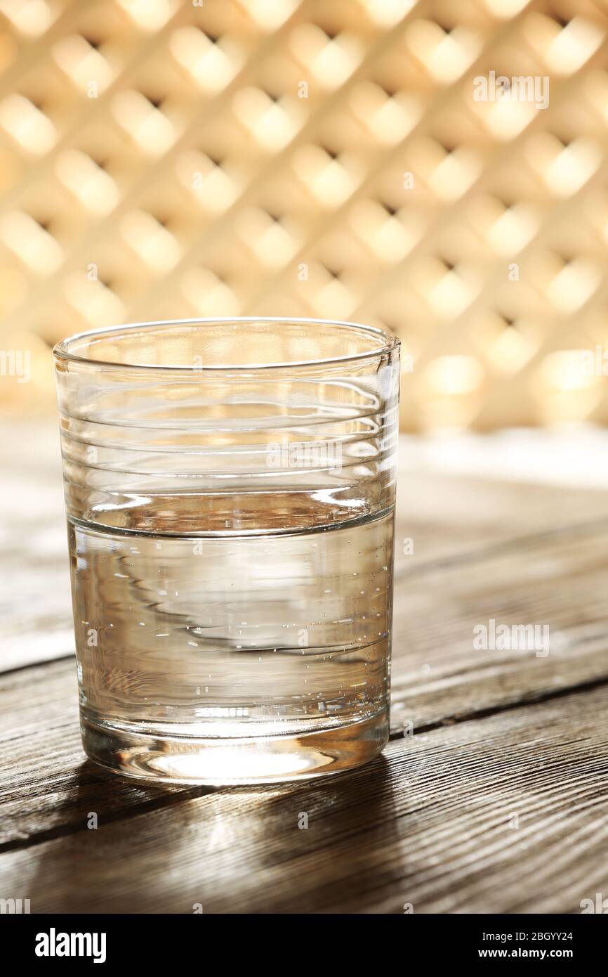 Glass of clean mineral water on wooden surface and lattice background ...